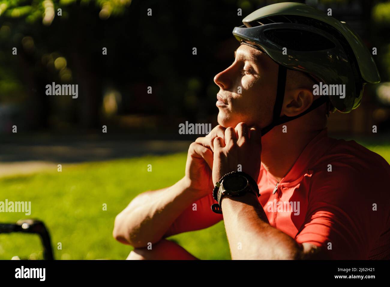 Young white cyclist wearing helmet while sitting on grass during ...