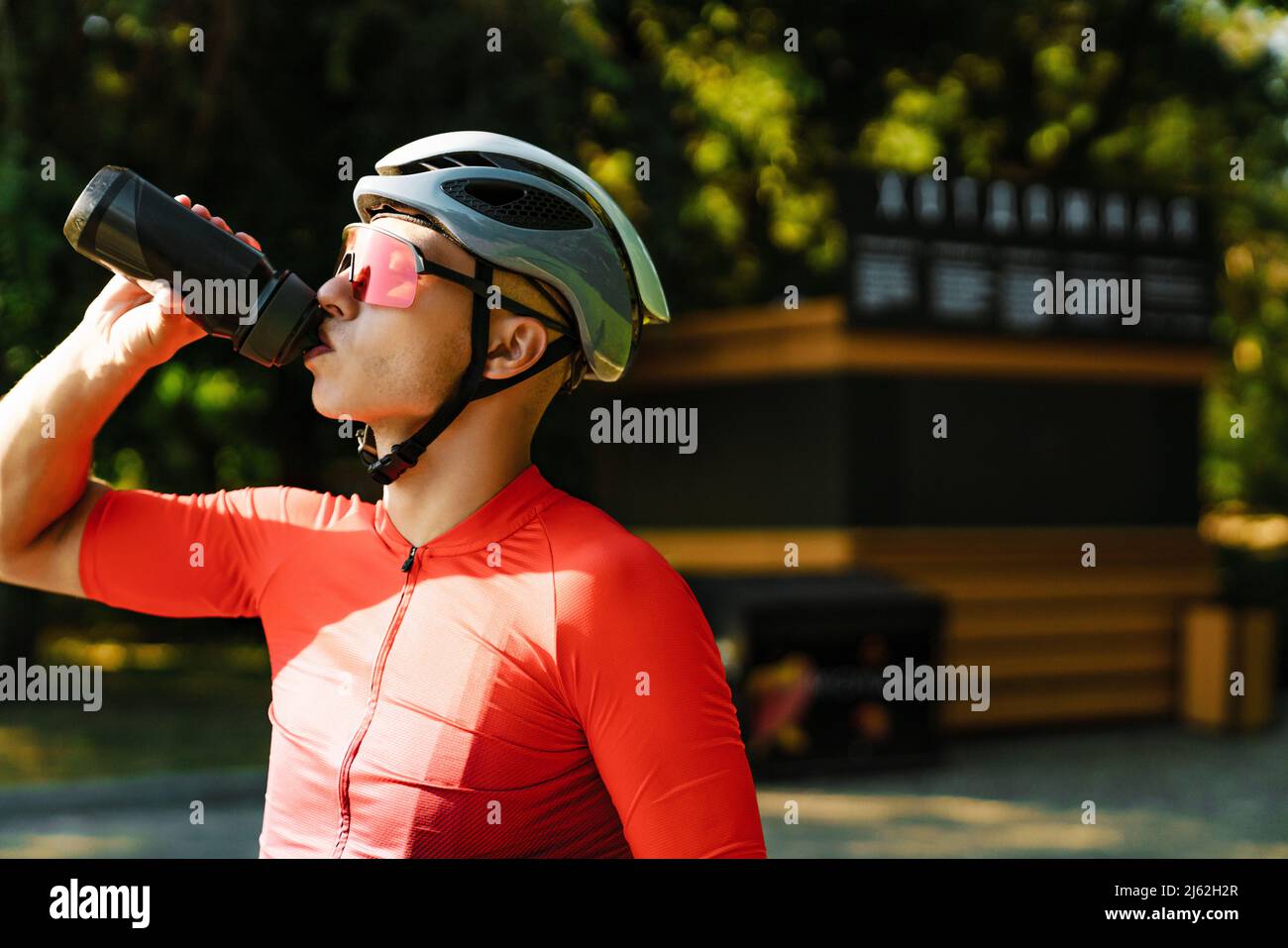 Young white cyclist in helmet drinking water during workout outdoors ...