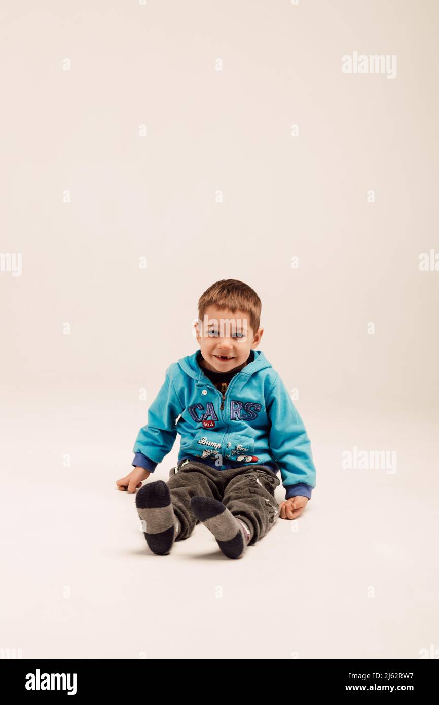 A little boy in a blue jacket sits on a white background Stock Photo ...