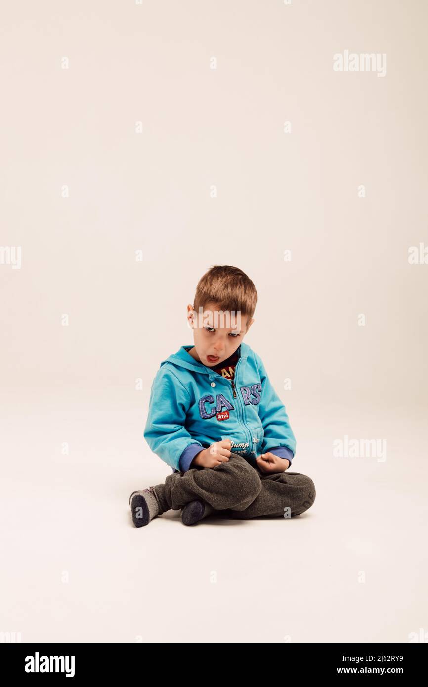 A little boy in a blue jacket sits on a white background Stock Photo ...