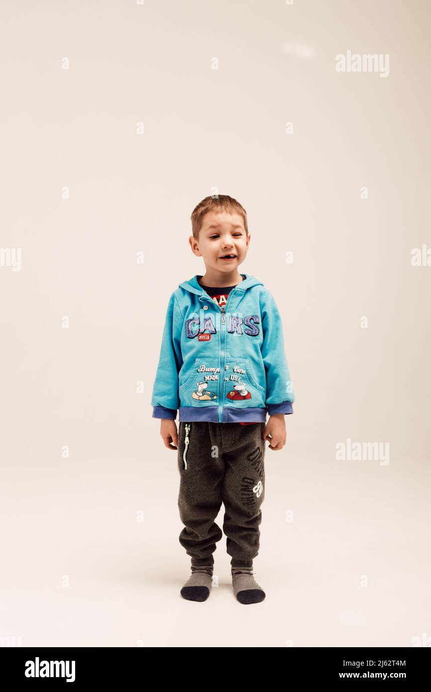 A little boy in a blue jacket stands on a white background and smiles ...