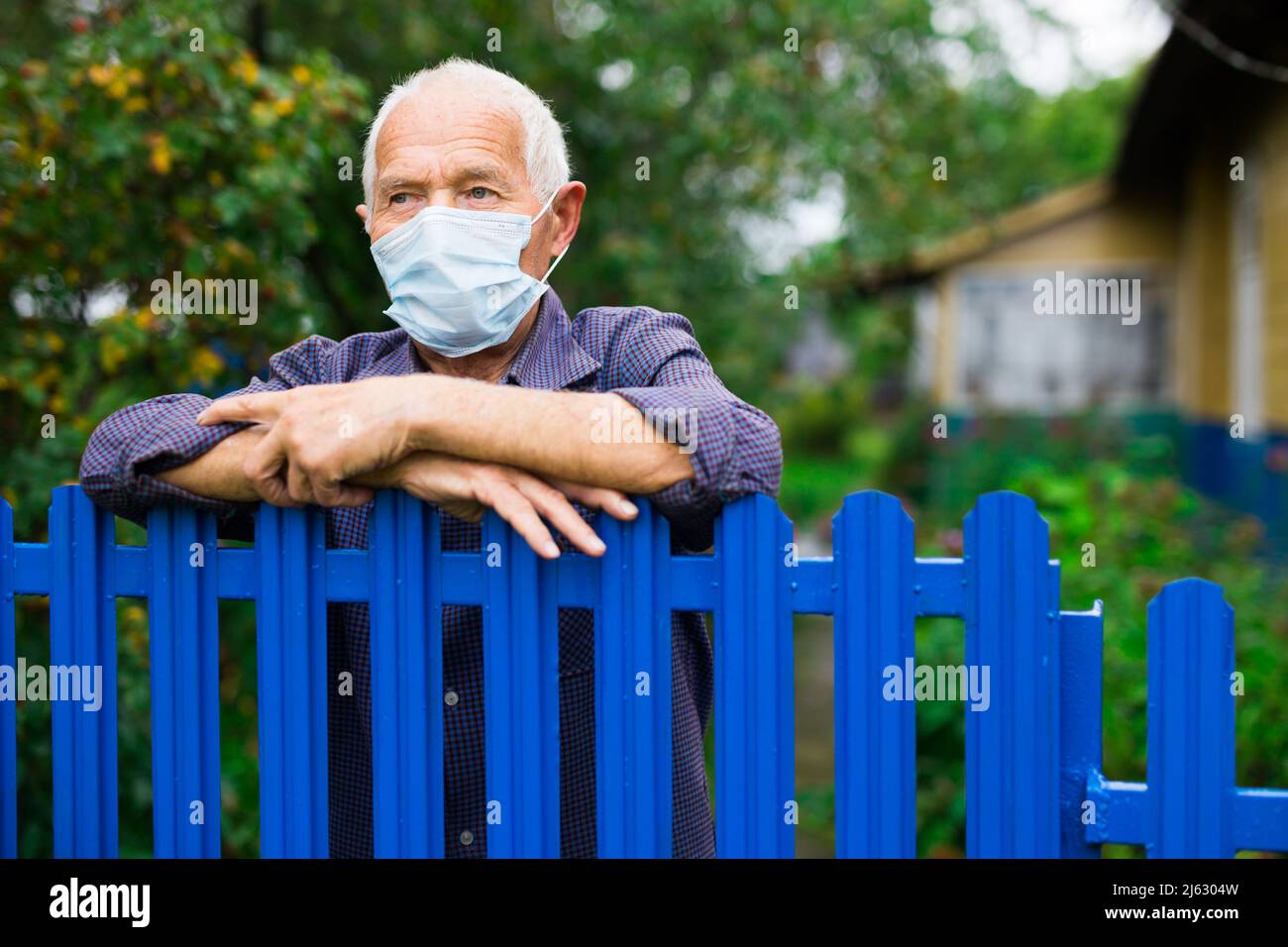 Portrait of gray-haired owner in protective mask at fence of his ...