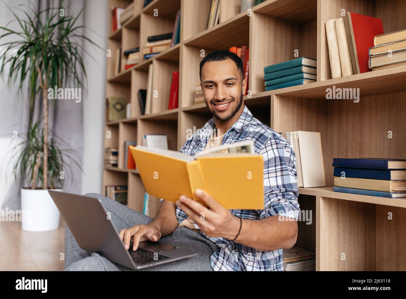 Happy arab man reading book near laptop computer, learning online while ...