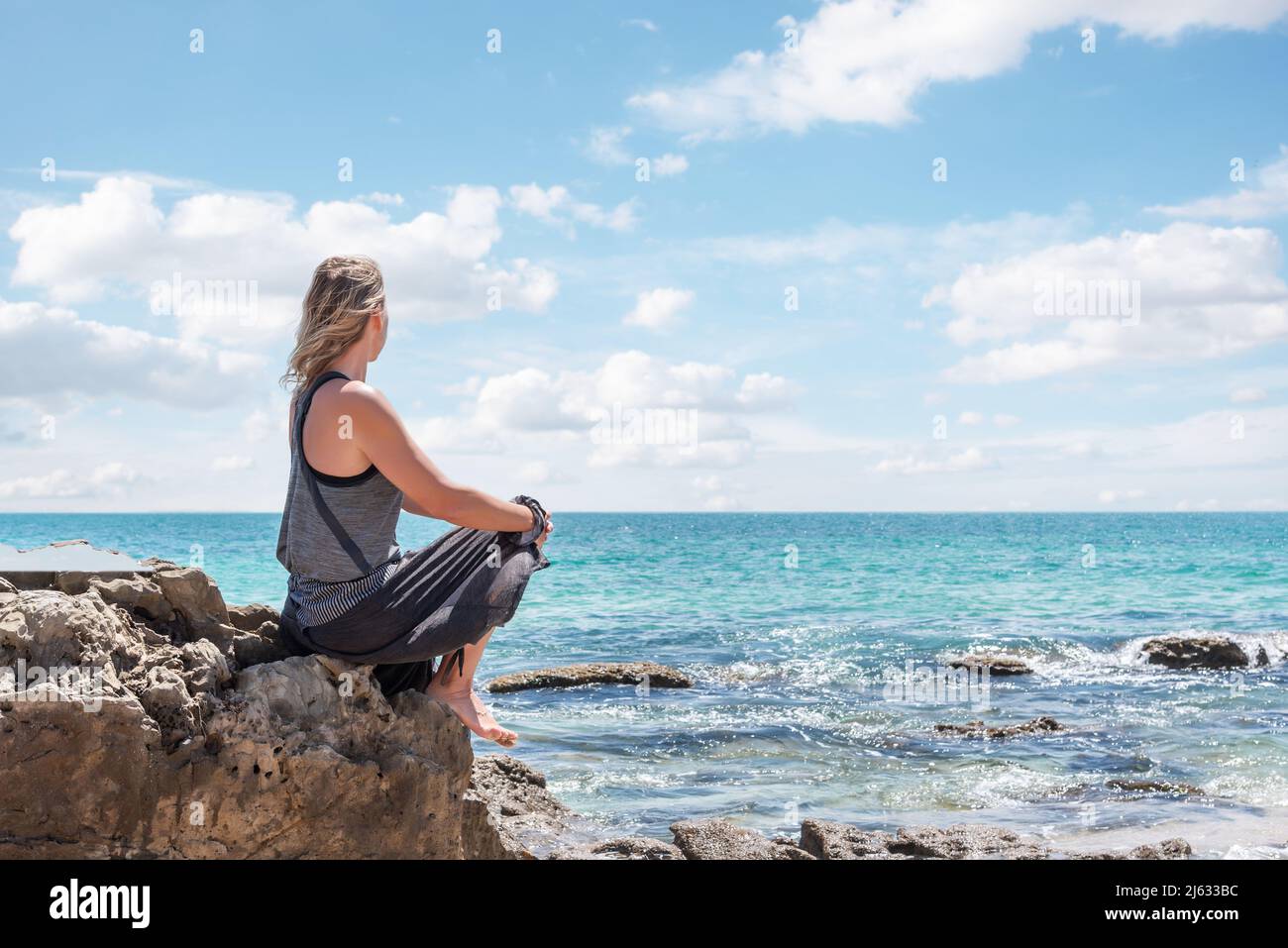Caucasian blonde woman sitting on a rock contemplating the sea ...