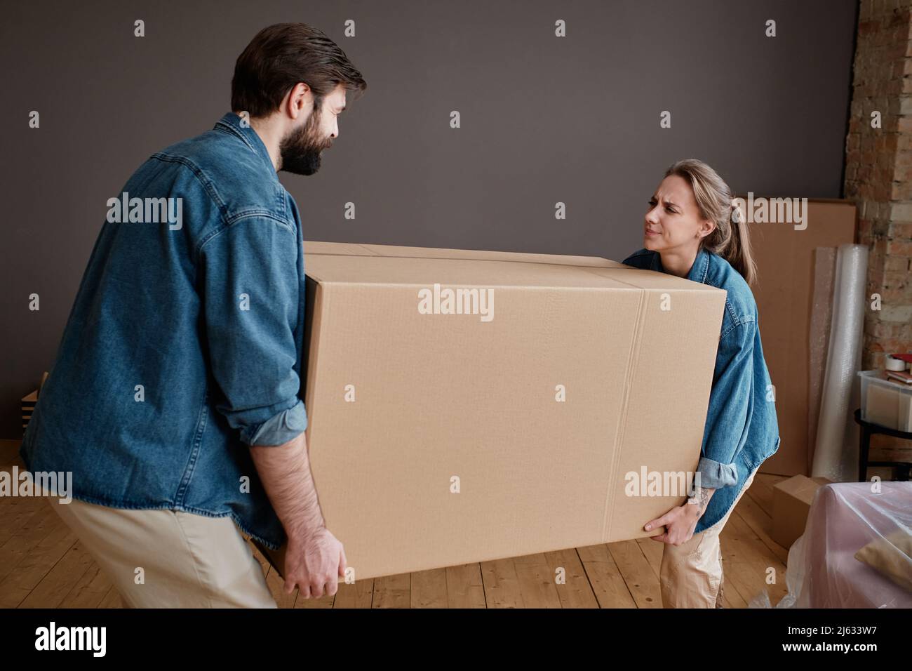 Horizontal shot of young man and woman moving to new apartment carrying ...
