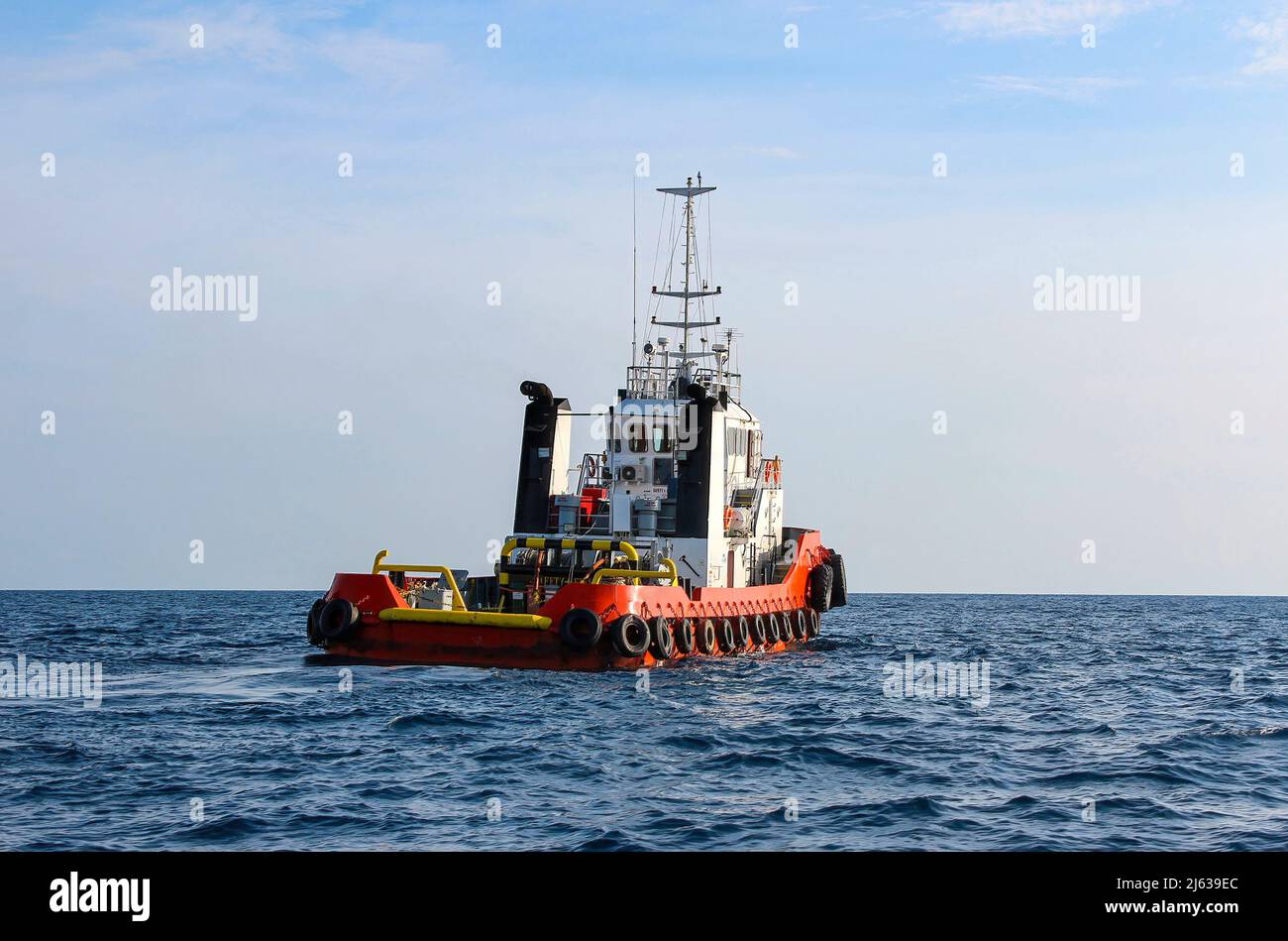 Red hulled tug boat with car tyres around it, moving ahead in open ...
