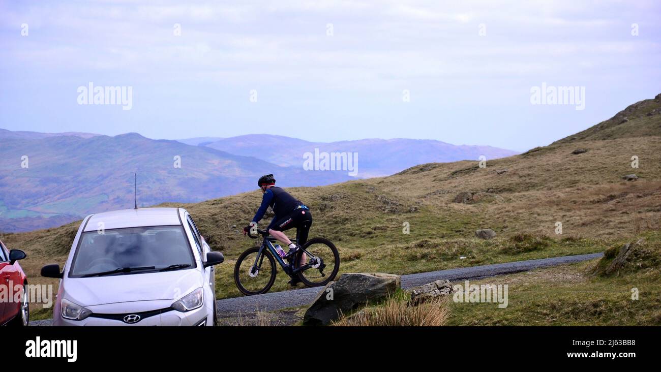 A cyclist passes cars parked near the top of Wrynose Pass, Lake ...