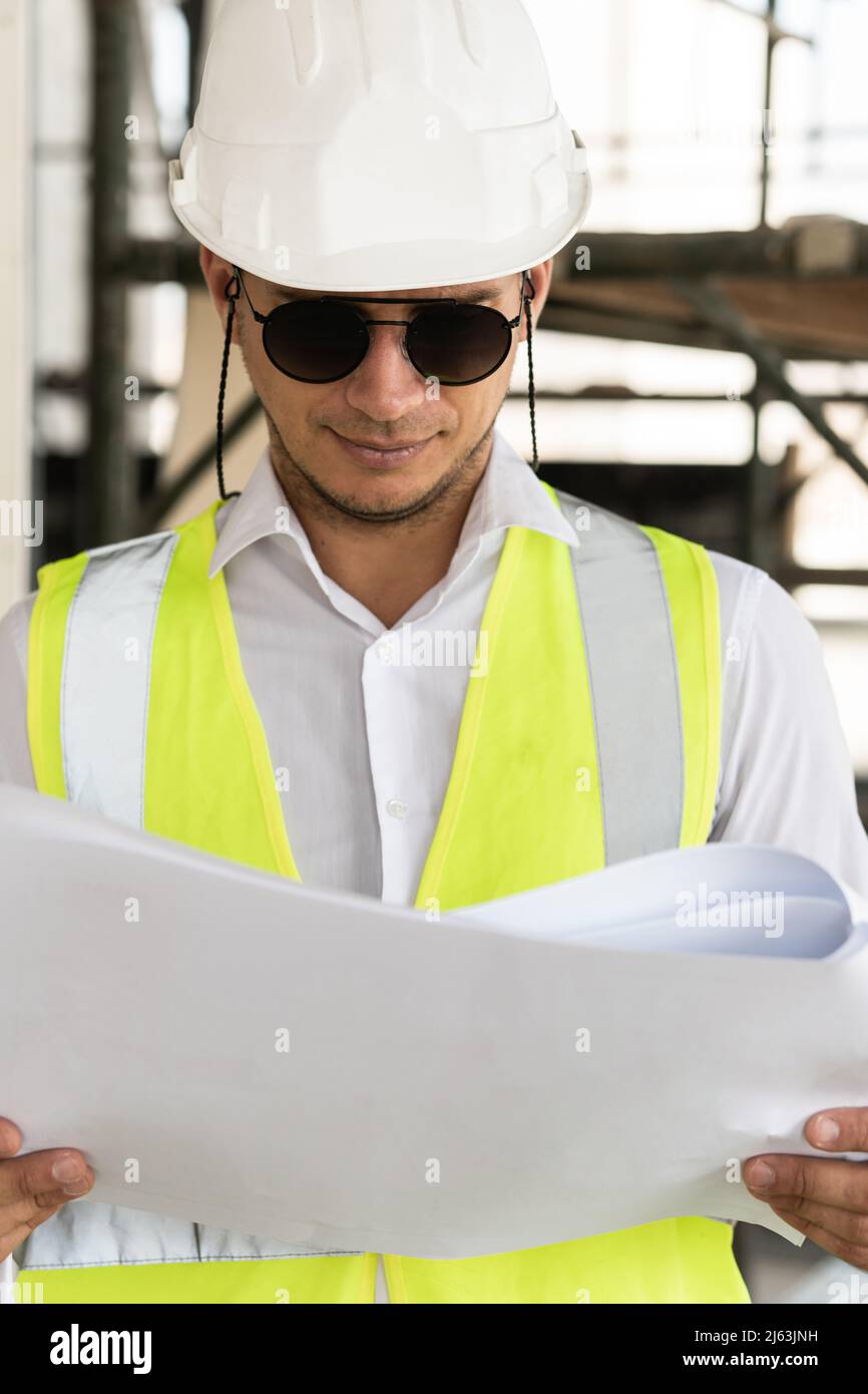 Man architect wearing safety vest with a blueprints on a construction ...