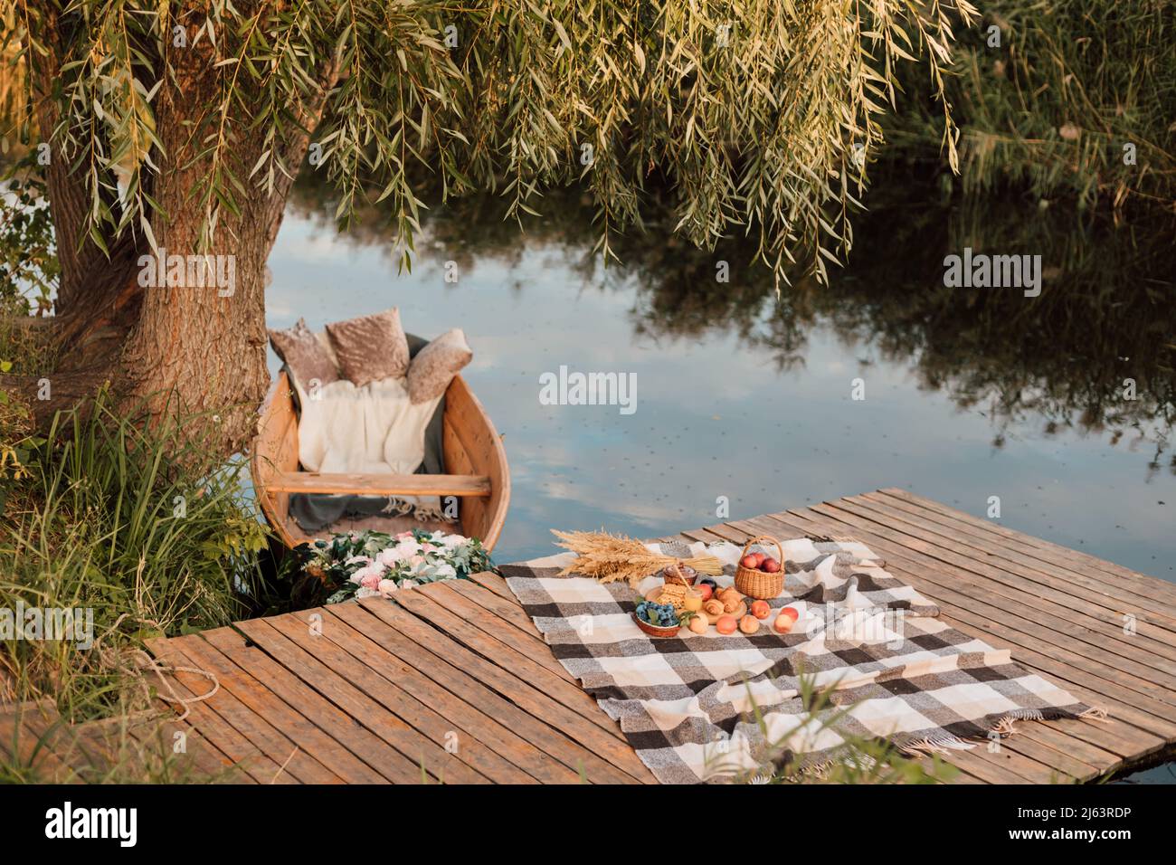 Beautiful wooden boat stands near the pier under a large willow tree ...