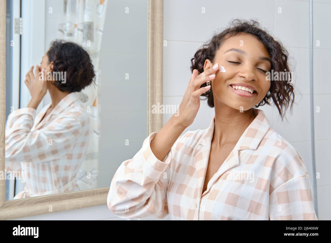 Happy african american woman applying moisturizer face cream on her ...