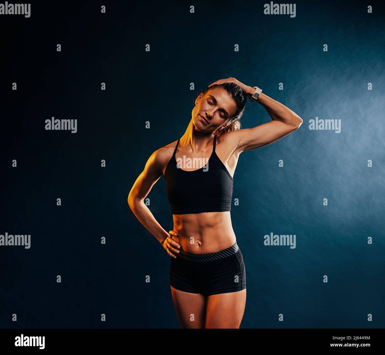 Young Muscular Woman Warming Up Her Neck Before Training Against Black
