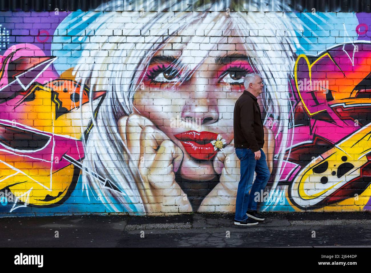 A middle aged man walking past a wall featuring colourful street art in ...