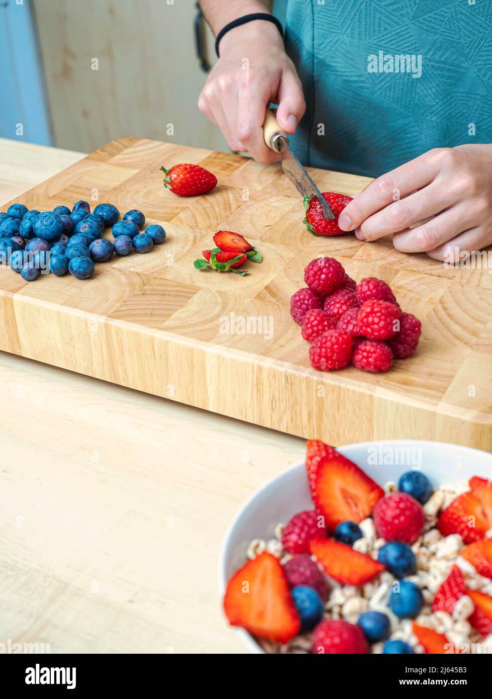 Woman in her kitchen, on a wooden table cutting fruit to prepare a ...