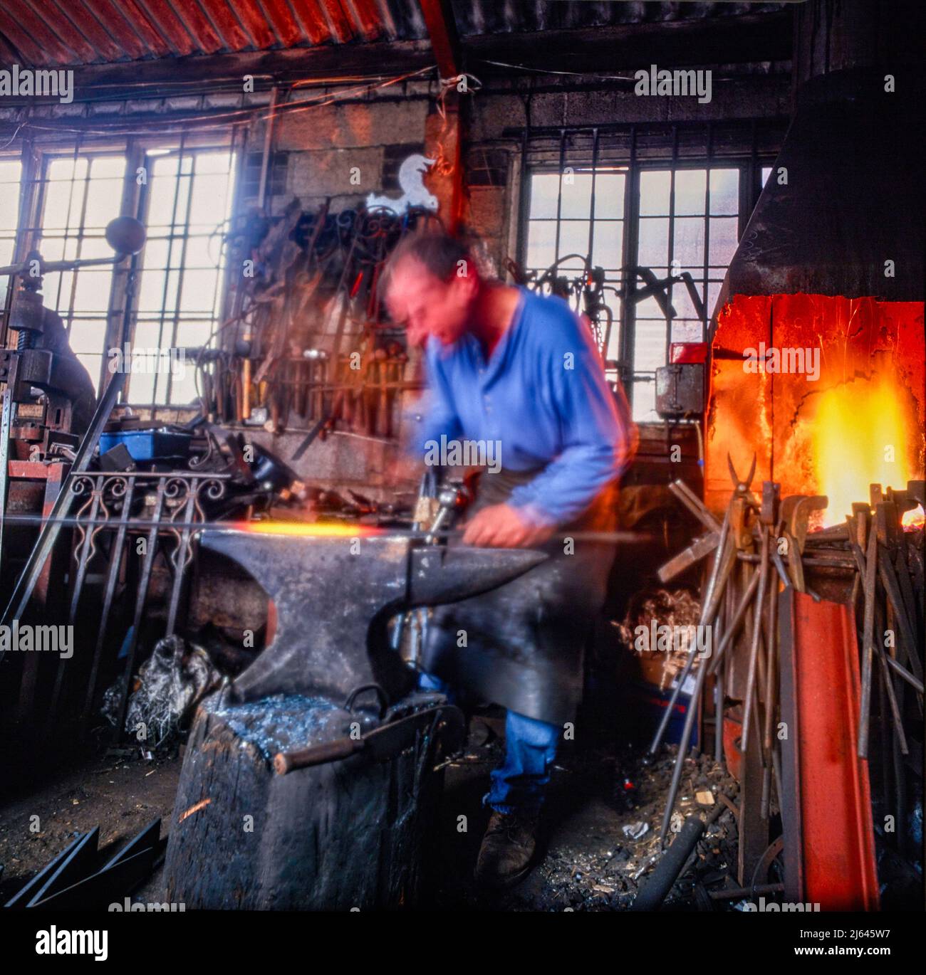 Traditional Blacksmith working at his anvil with flames in the ...