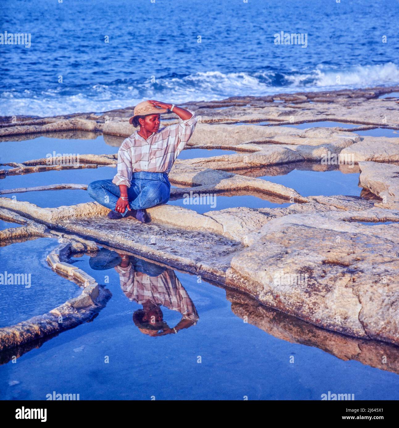 Black female holidaymaker reflected in a pool at low tide, seashore of ...