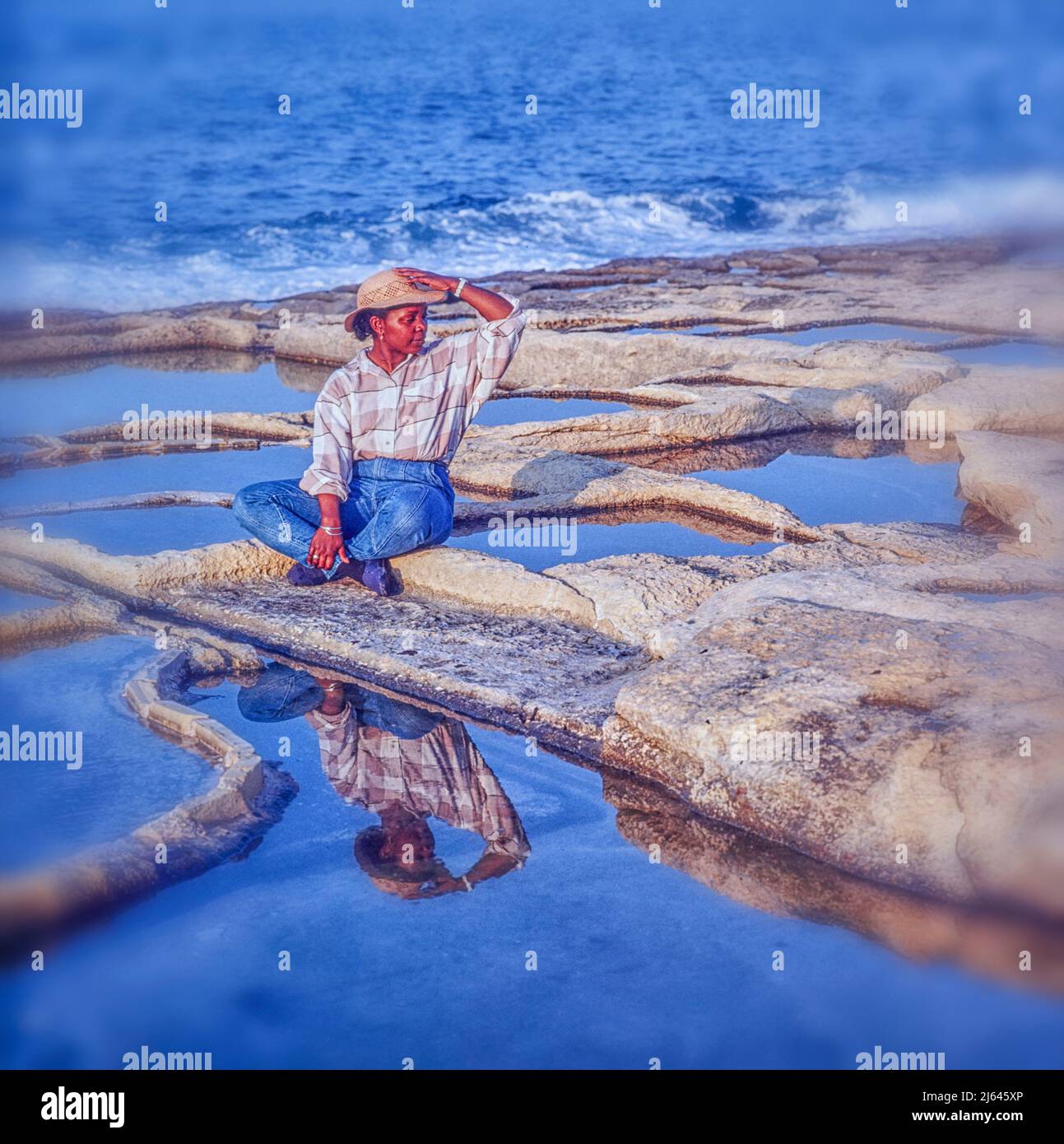 Black female holidaymaker reflected in a pool at low tide, seashore of ...