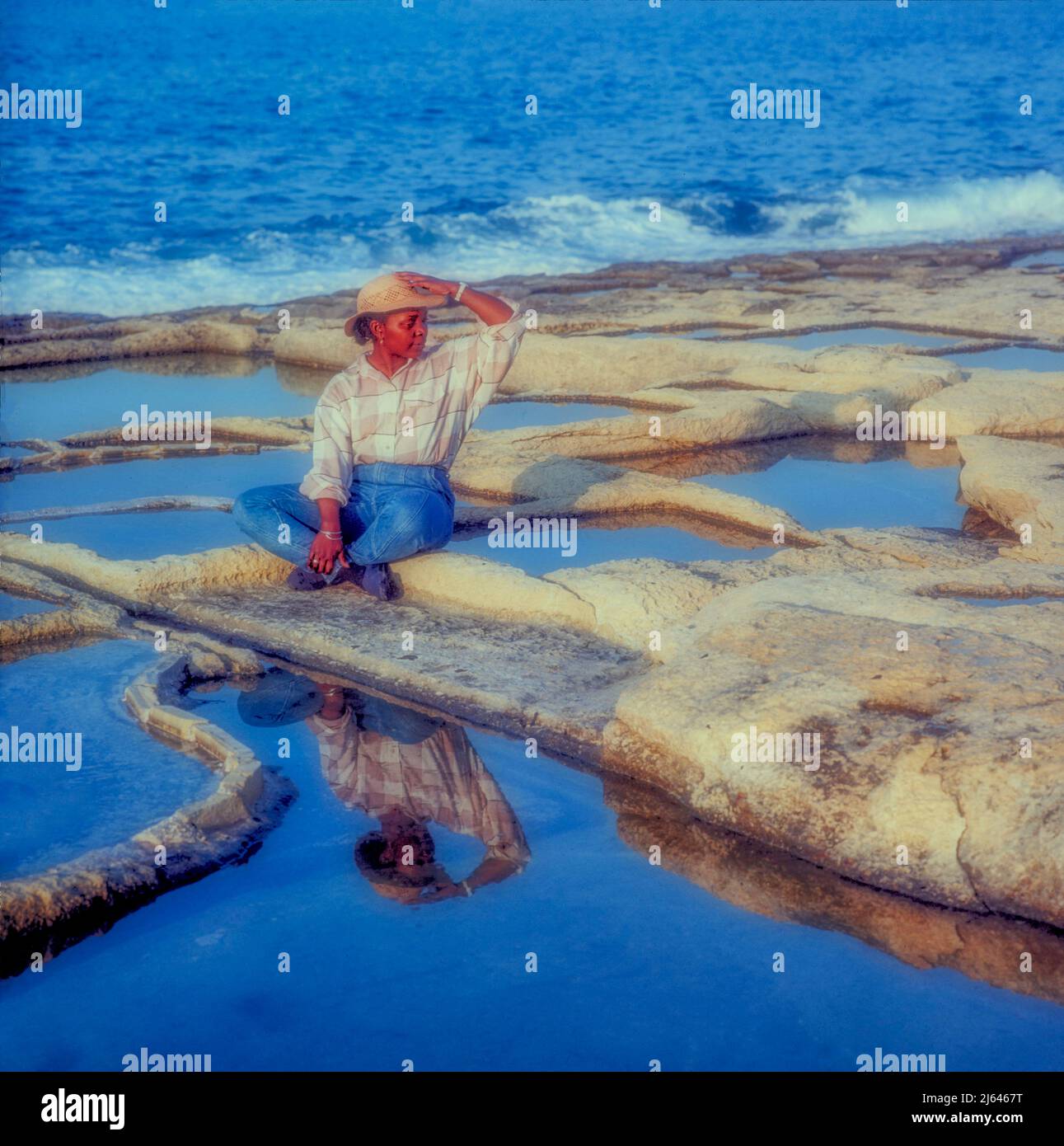 Black female holidaymaker reflected in a pool at low tide, seashore of ...