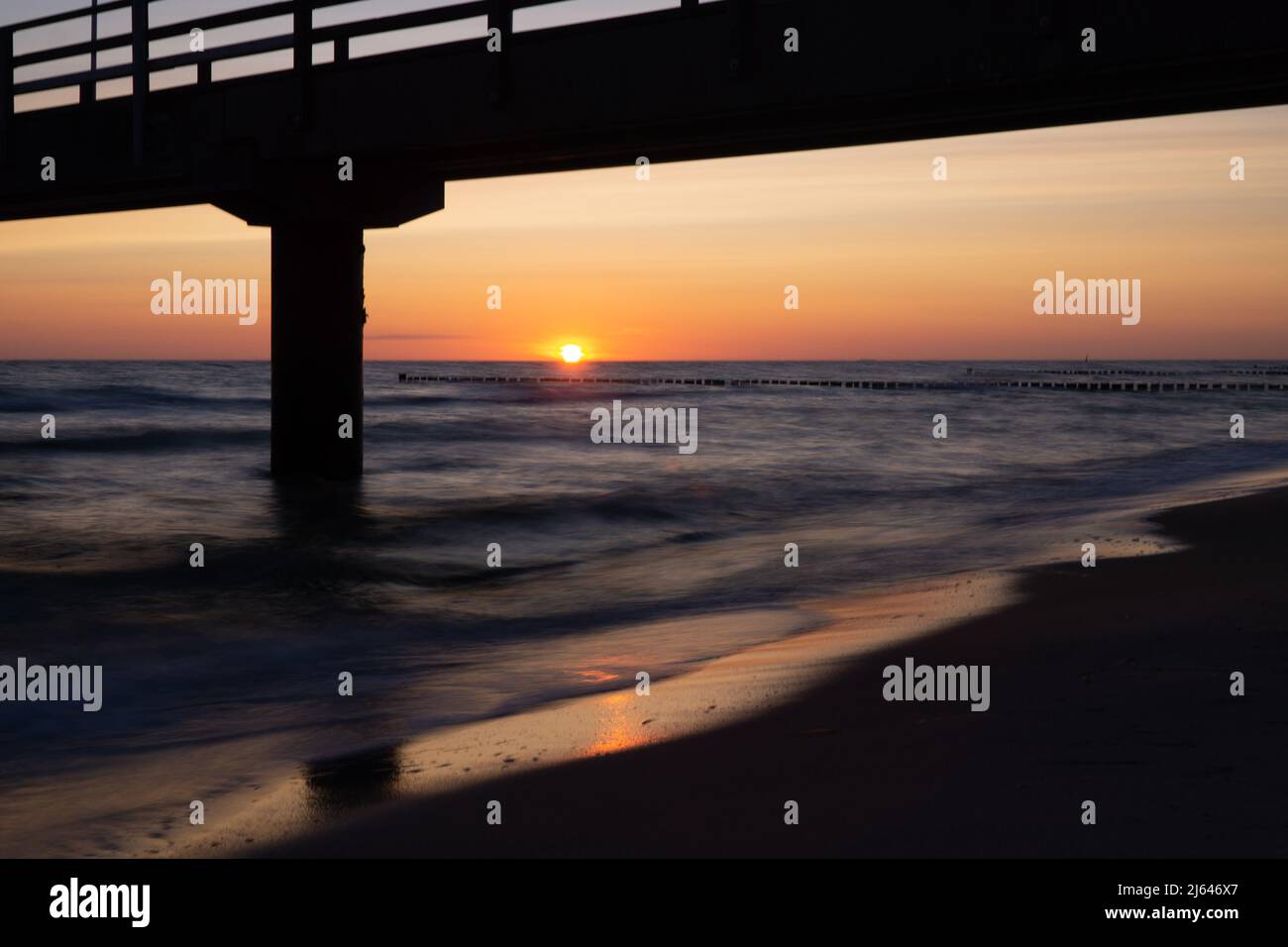 A beautiful golden sunrise at a pier at the beach in Zingst germany ...