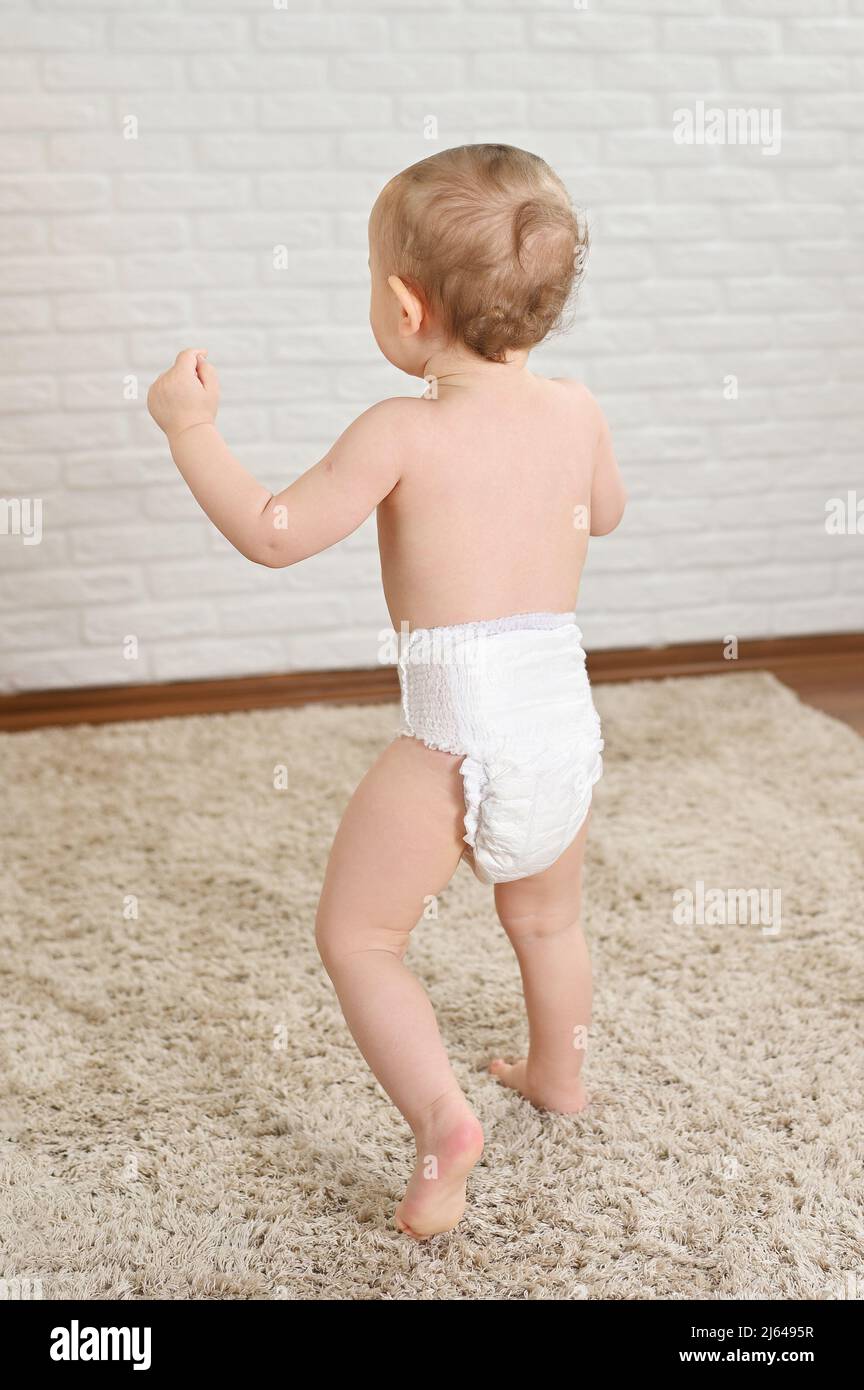 small child in a disposable diaper against a white wall - view from the ...