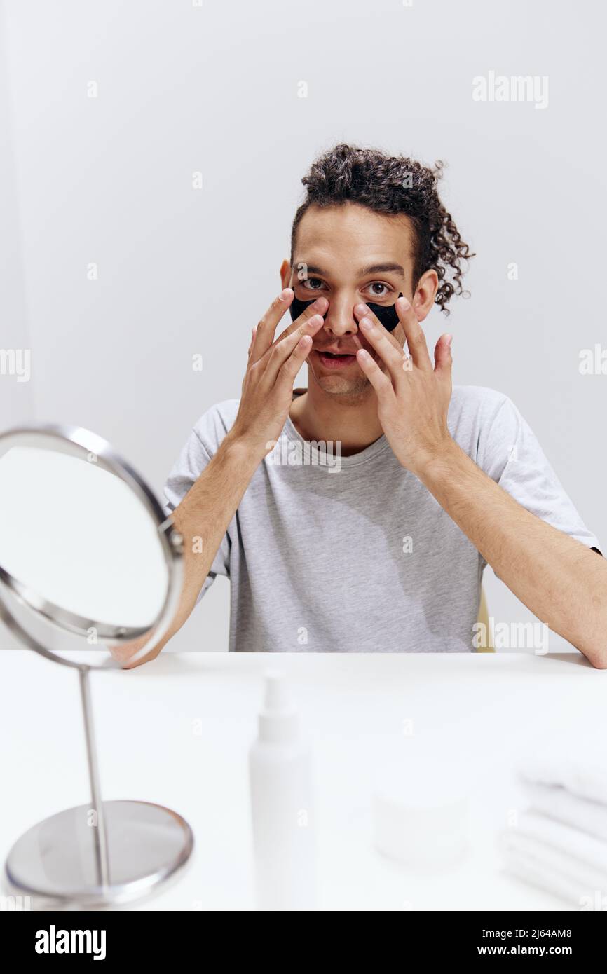 A young man with patches on the face sit in front of the mirror light ...