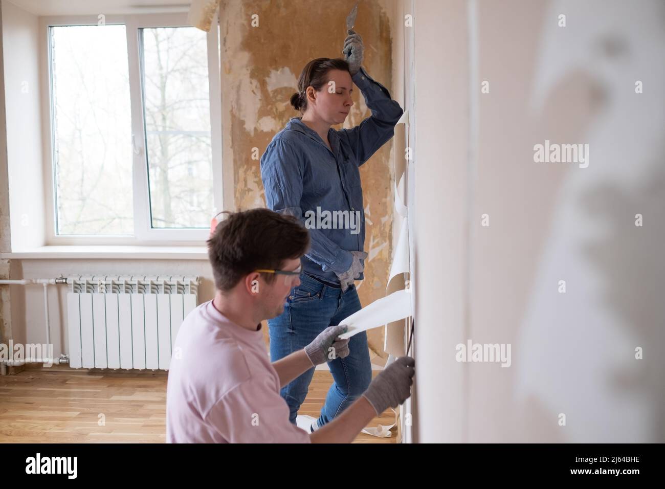 Young caucasian couple removing old wallpaper from walls preparing for ...
