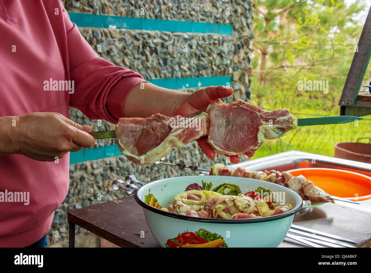 A bowl filled with marinated raw meat and women's hands stringing ...