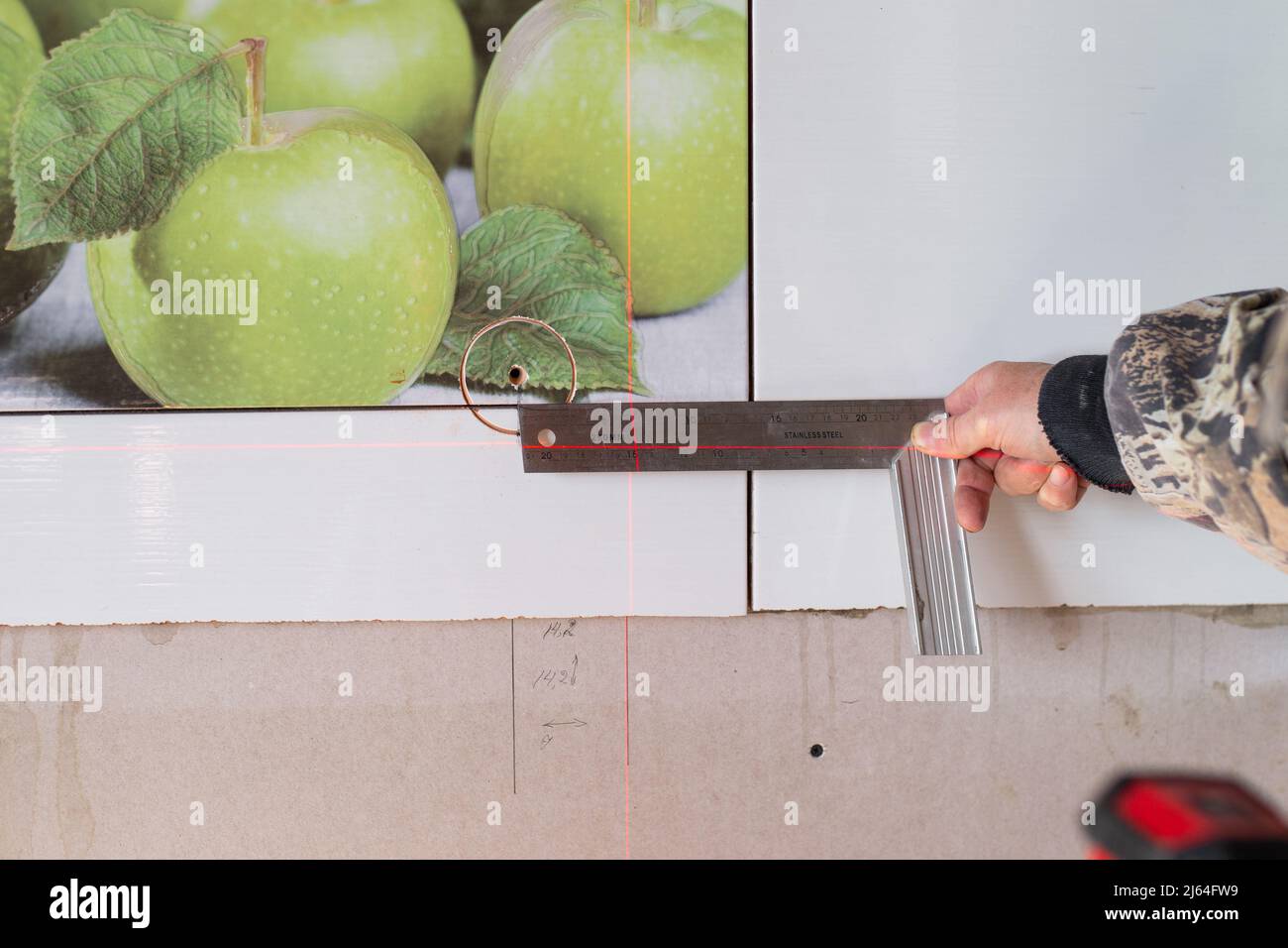 A man using a laser level and a ruler makes markings for the opening of ...