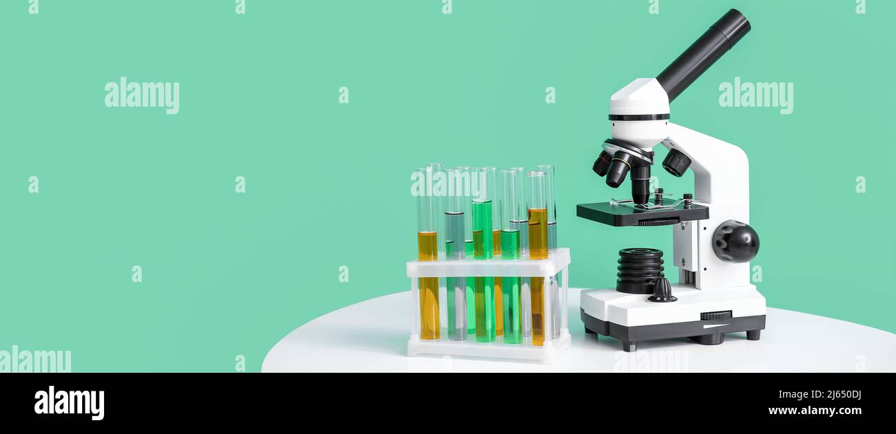 Modern microscope and test tubes on table against green background with ...