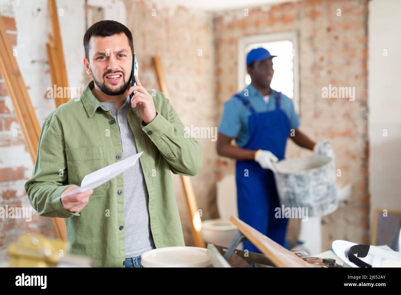Engineer holds an estimate in his hands, talking on a mobile phone ...