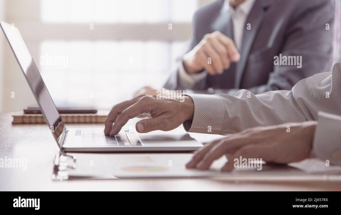Two businessmen with laptop computer reviewing financial statements for ...
