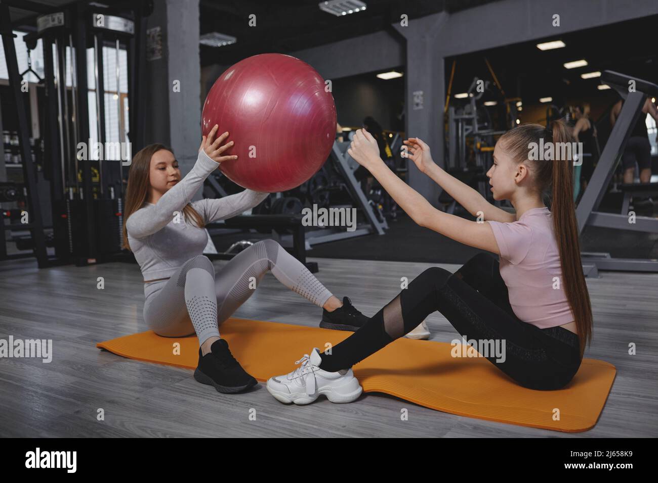 Young girl exercising with her personal trainer, using fit ball, doing ...