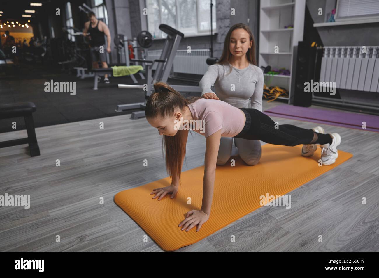 Teen girl doing plank exercise under personal trainer supervision at ...