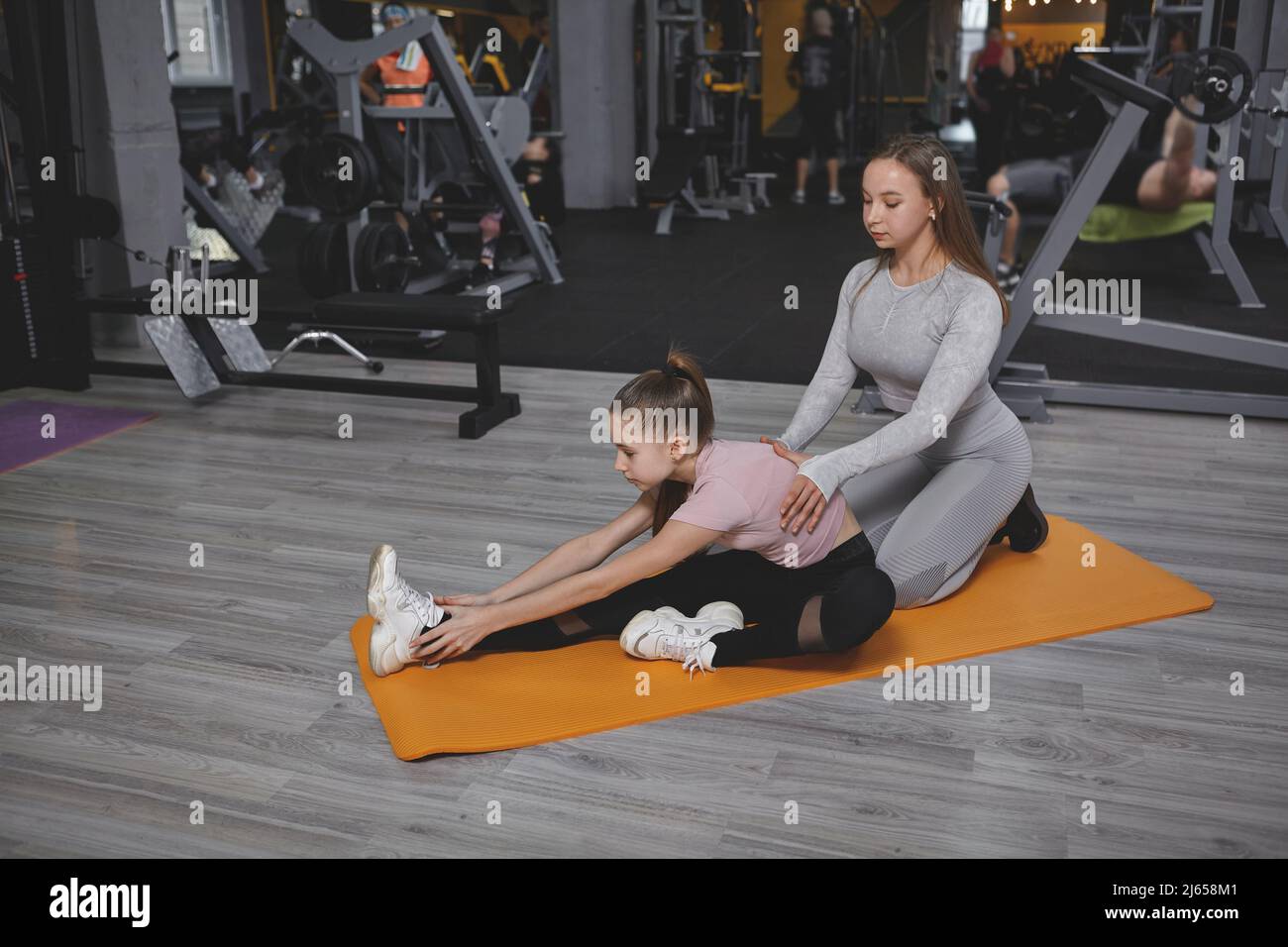 Professional gym coach helping her teen client stretching before ...