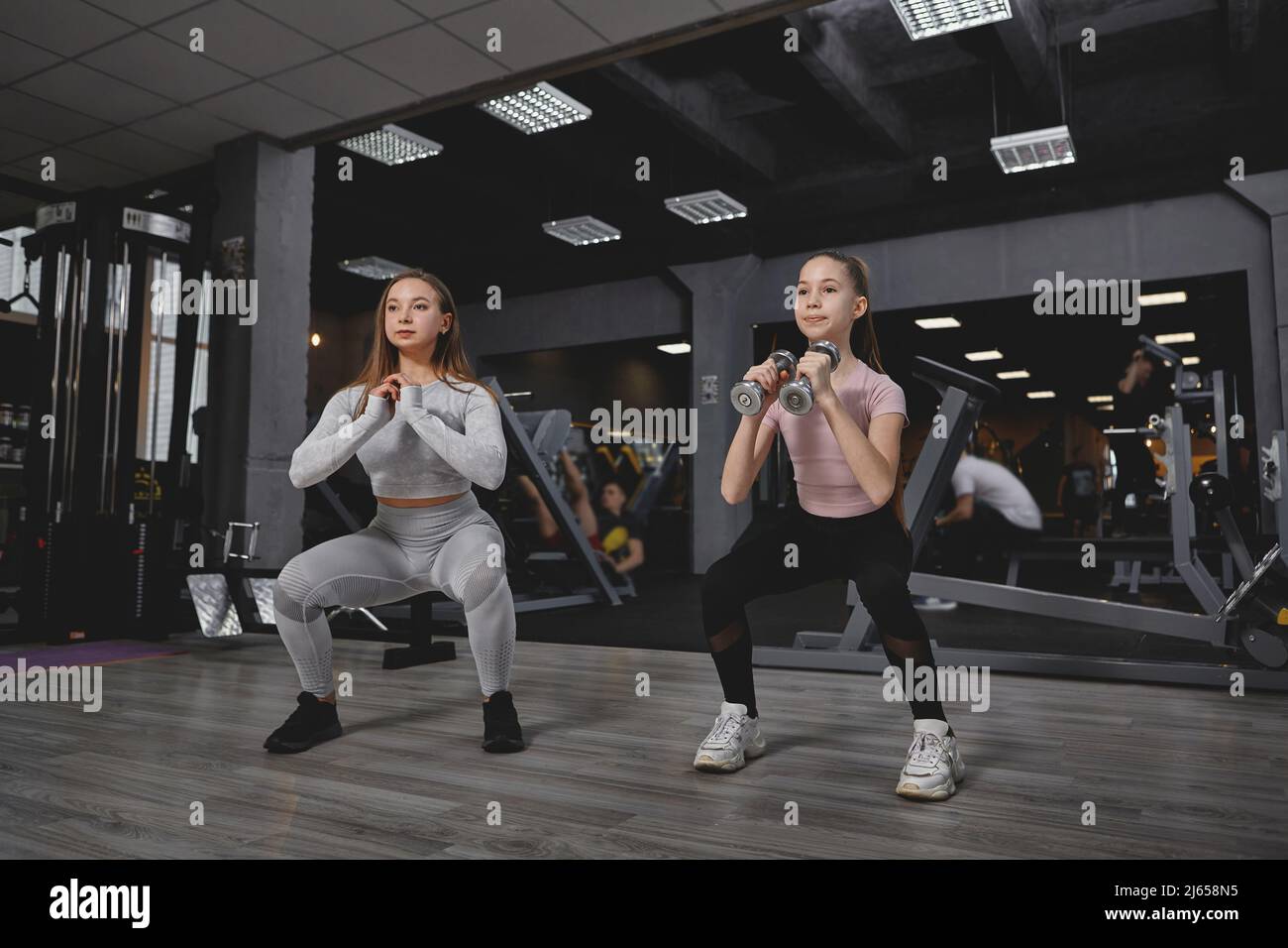 Personal trainer and her teenage female client doing squats with ...