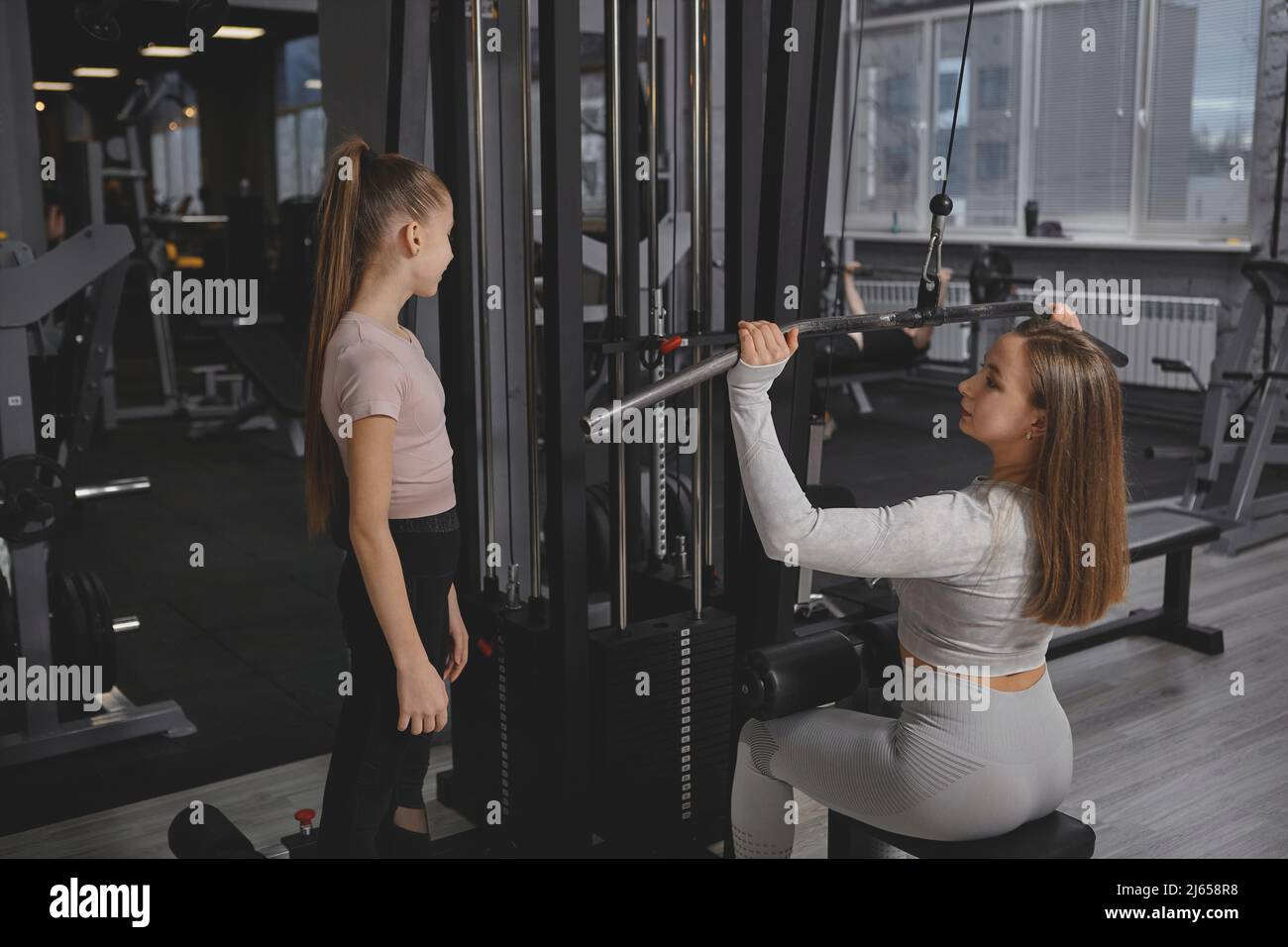 Personal trainer teaching teen girl working out on lat pull down gym ...