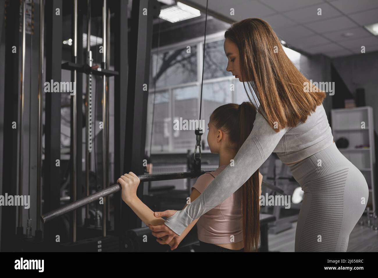 Rear view shot of personal trainer helping teenage girl exercise on lat ...
