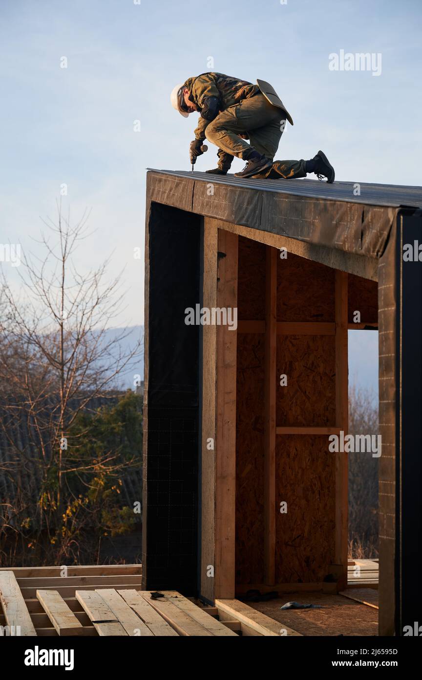 Male builder installing black corrugated iron sheet used as facade of ...