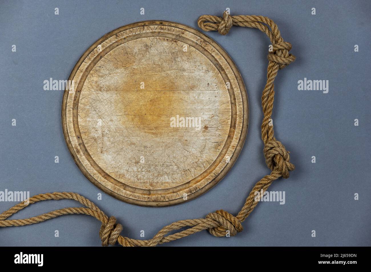 Round wooden cutting board and ship's rope against the gray background ...