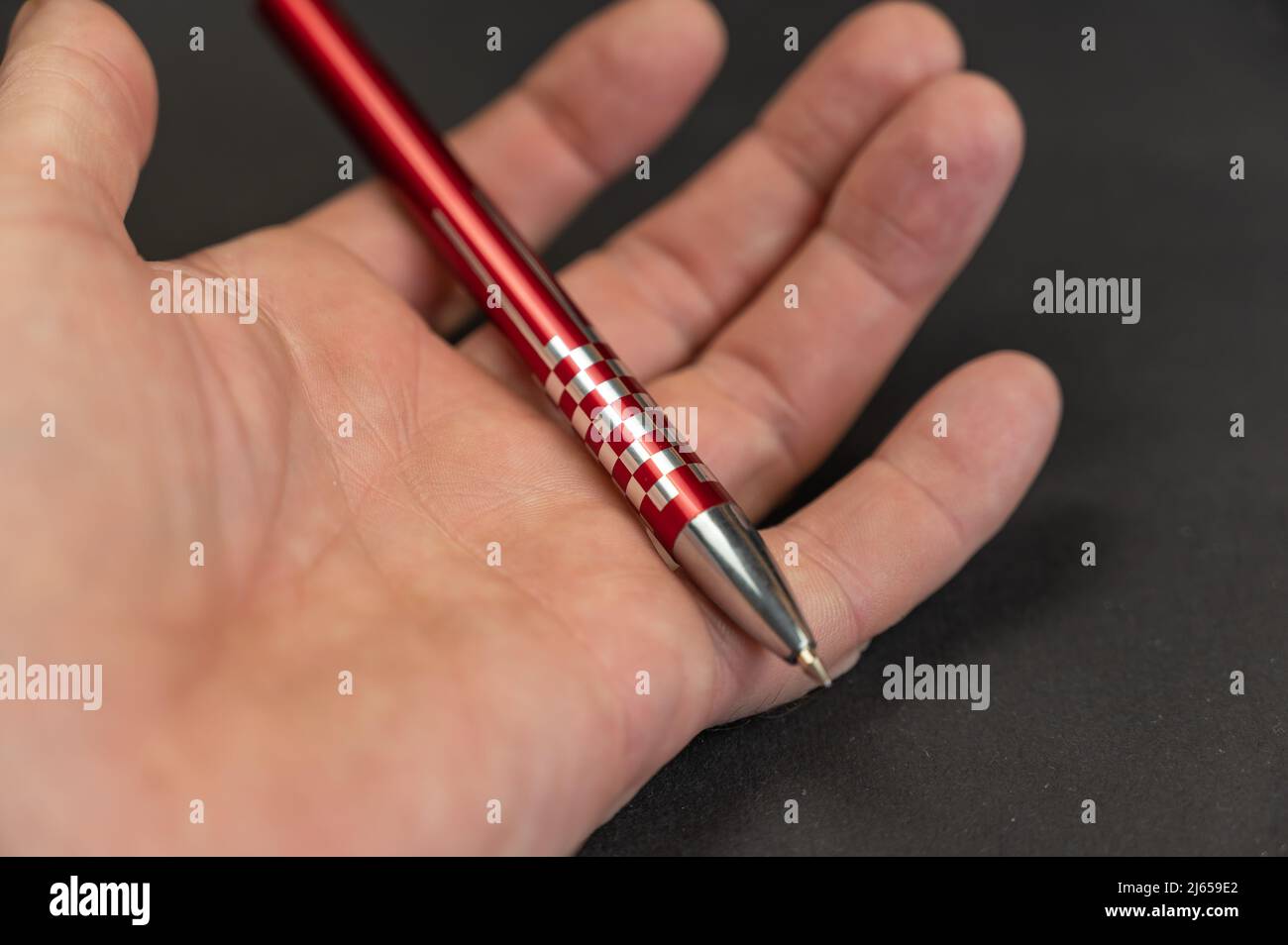 A close-up of a man's hand holding a red pen against a black background ...