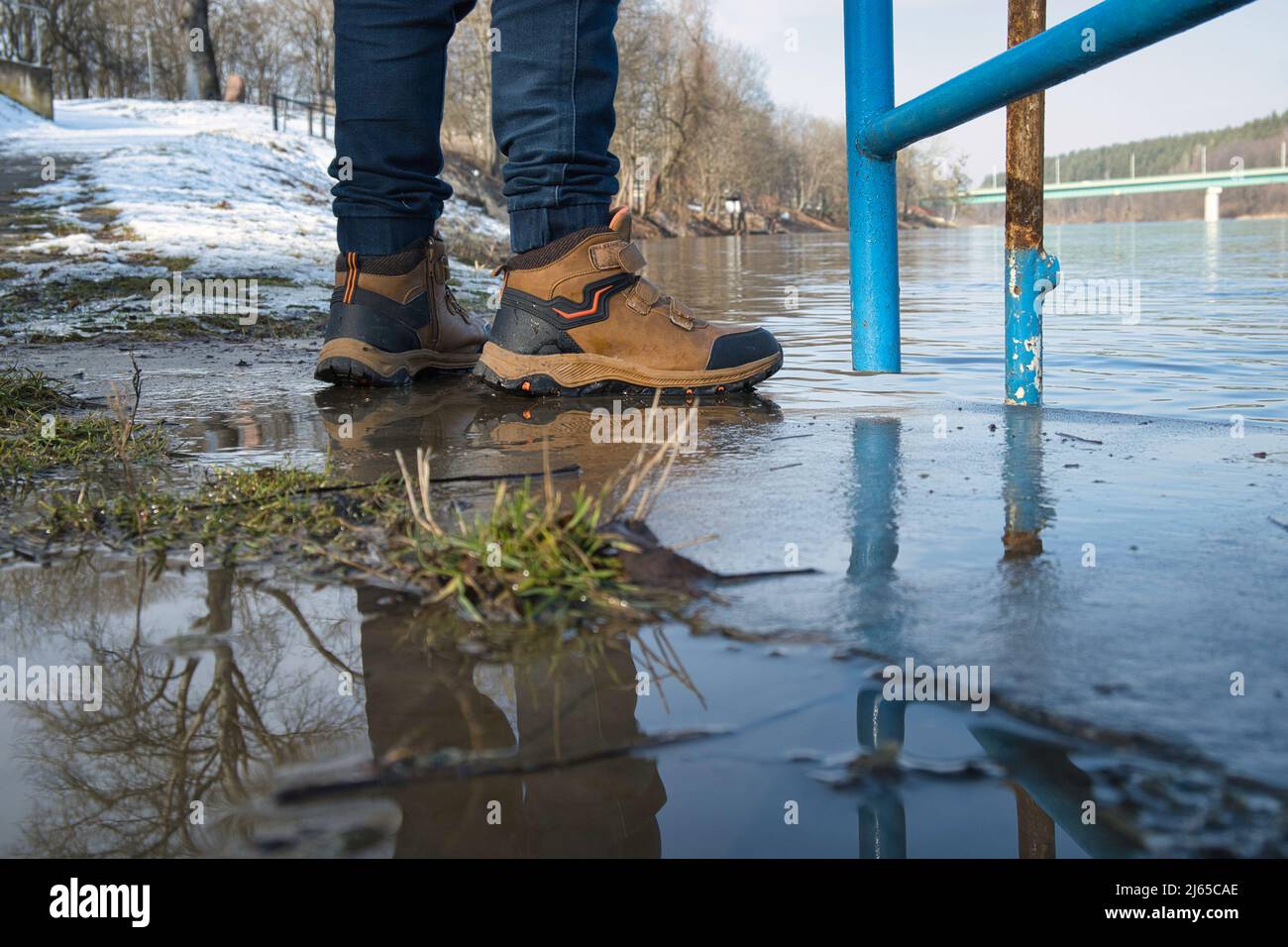 Spring flooding, person wearing hiking boots standing on wet paving ...