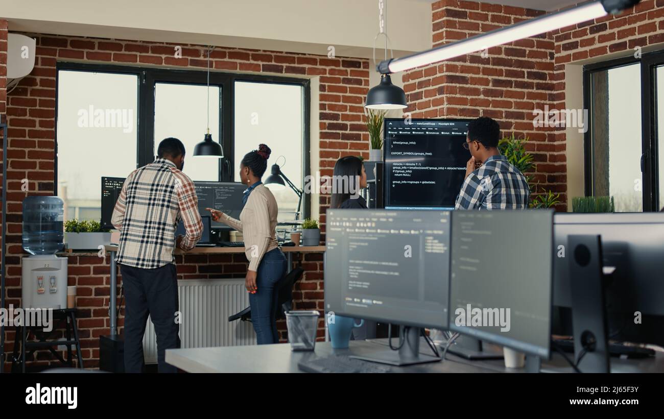 System Developers Analyzing Code On Wall Screen Tv Looking For Errors While Team Of Coders