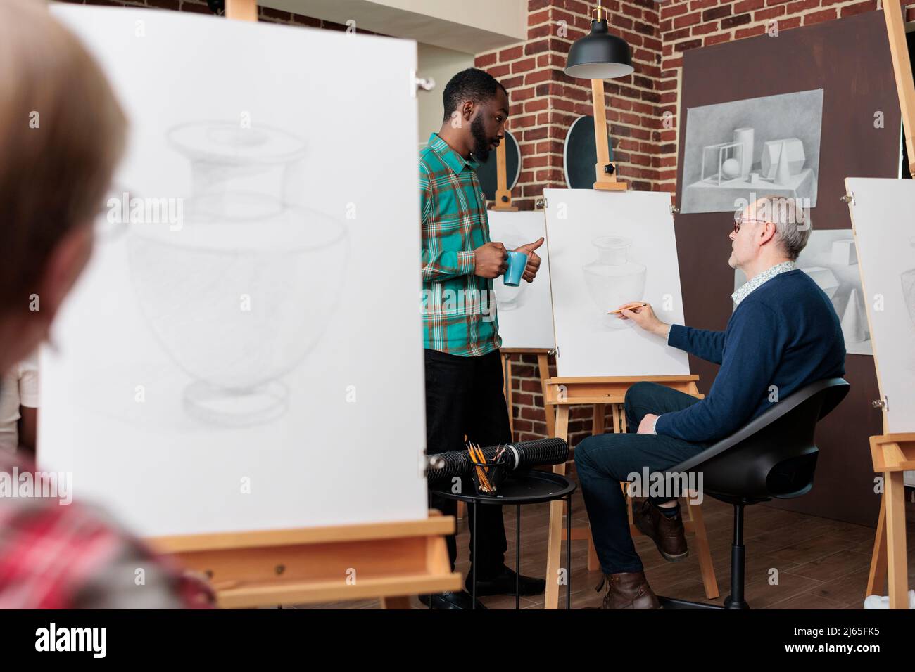 Young painting teacher explaining graphic technique to student working ...