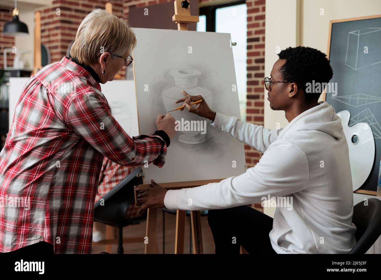 Senior teacher explaining sketching technique to african american ...