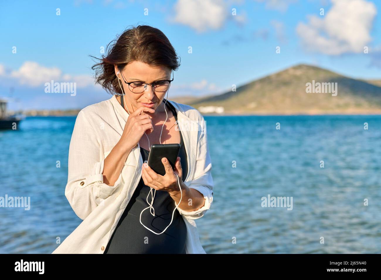 Happy 40s age woman in headphones with smartphone on the beach Stock ...