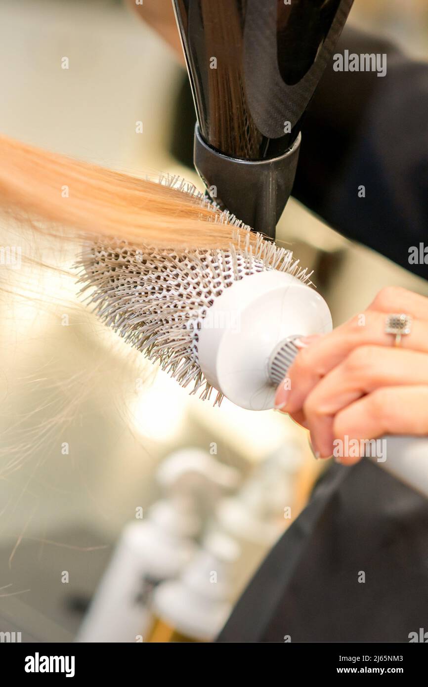 Drying straight blond hair with black hairdryer and white round brush ...