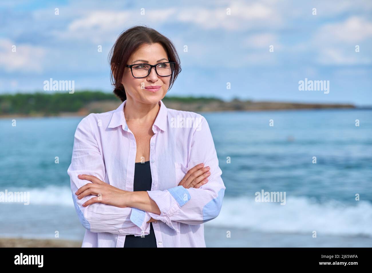 Smiling middle aged woman with folded hands, sea nature sky background ...