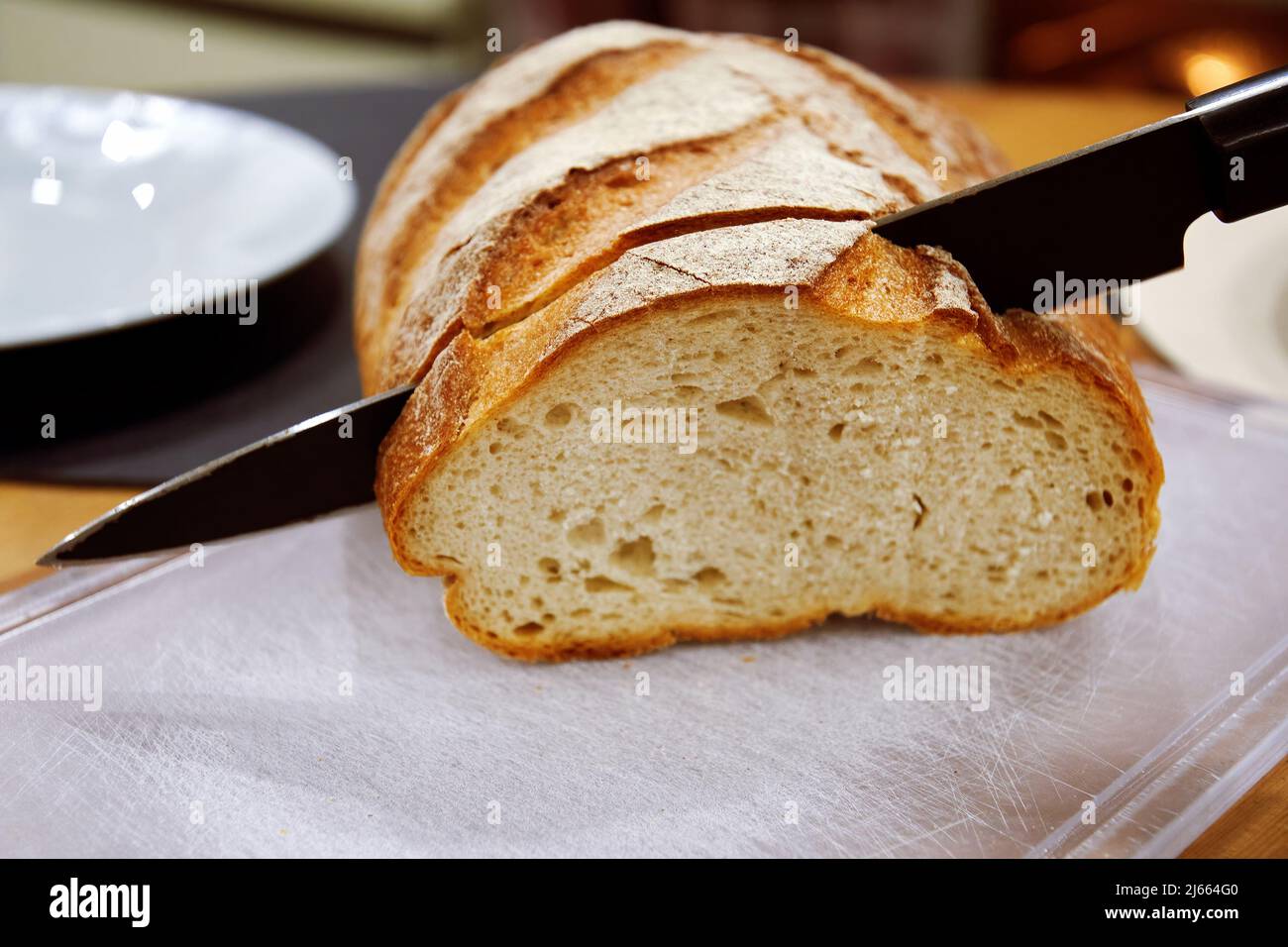 Sharp black knife cut the fresh bread on the table. Kitchen background ...