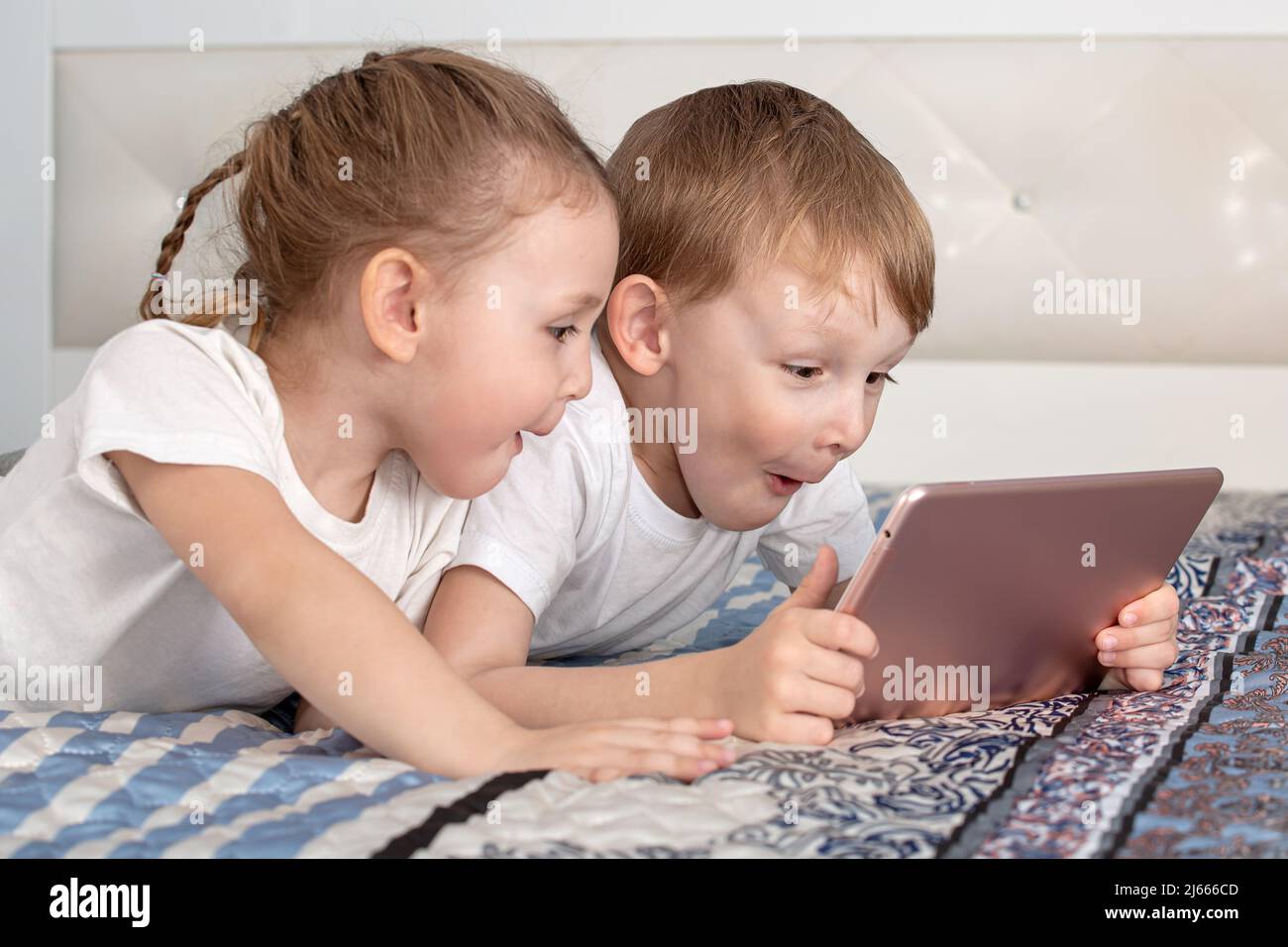 Kids and gadgets. A boy and a girl are lying on the bed and looking at ...