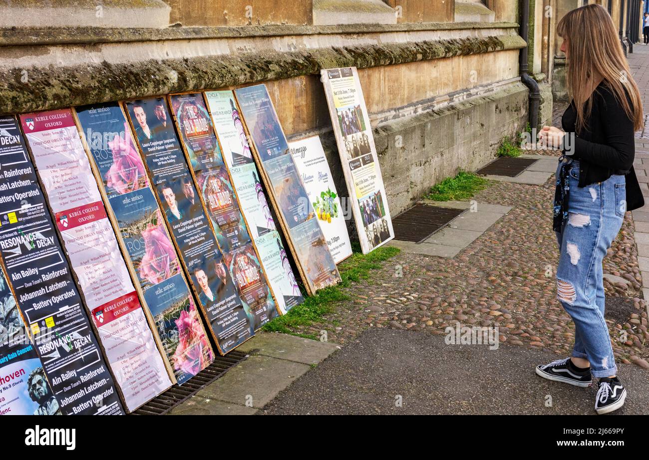 Young woman looking at a display of posters advertising music and drama ...