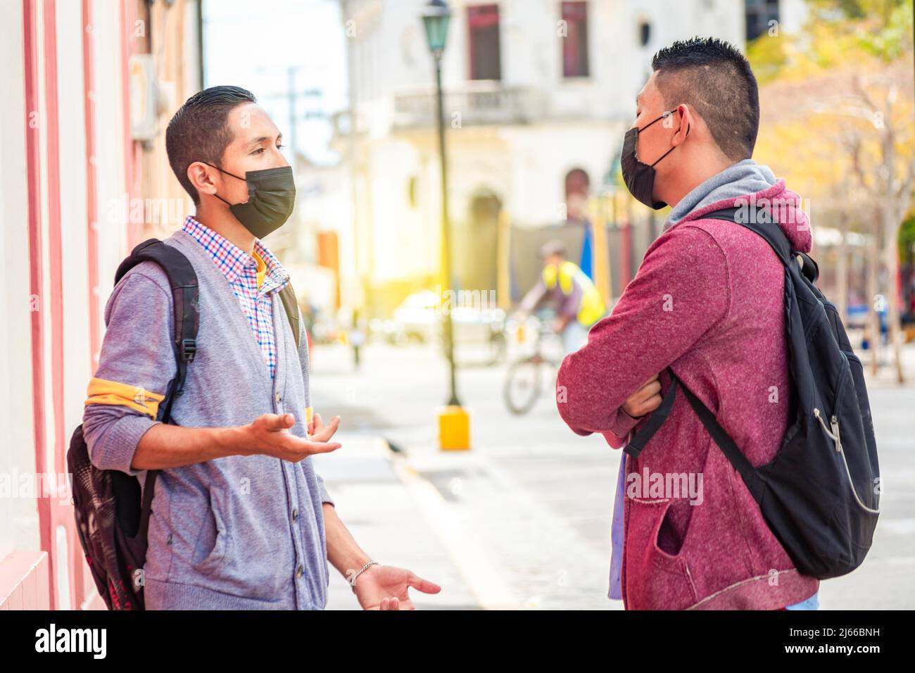 Two young people with mask having a conversation outdoors, two friends ...